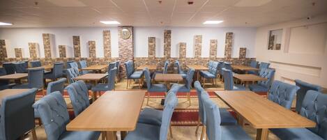 Uma sala de conferências com várias mesas e cadeiras estofadas azuis, dispostas em fileiras.