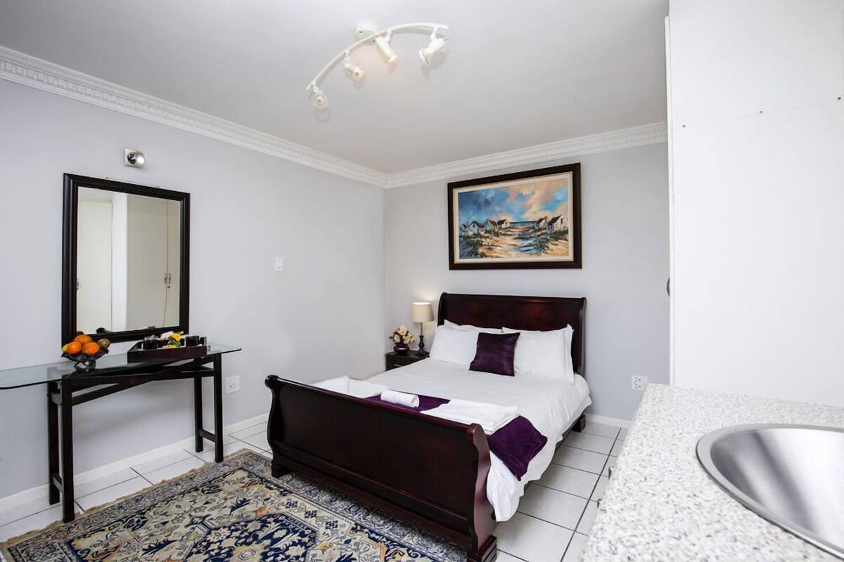 Quarto com cama, mesa de cabeceira, espelho, quadro e pia.