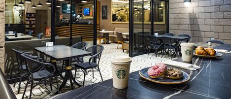 Um café acolhedor com mesas e cadeiras, uma xícara da Starbucks e doces sobre uma mesa.