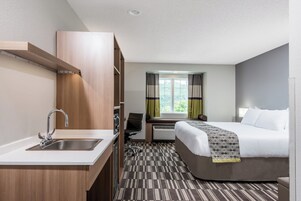 Quarto de hotel com cozinha compacta, uma cama, janela com cortinas e piso coberto por carpete.