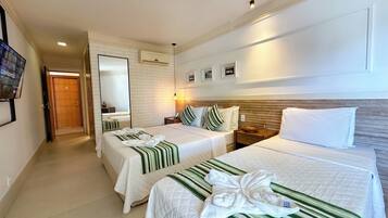 Quarto de hotel com duas camas, um espelho grande e cabeceira de madeira.