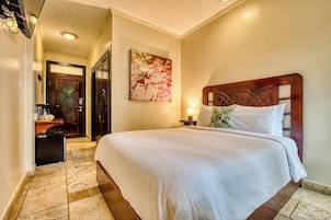 A hotel room with a large bed, a wooden headboard, a nightstand with a lamp, and a painting on the wall.