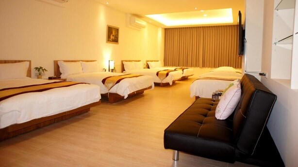 Quarto de hotel com quatro camas de solteiro, um sofá e uma TV fixada na parede.