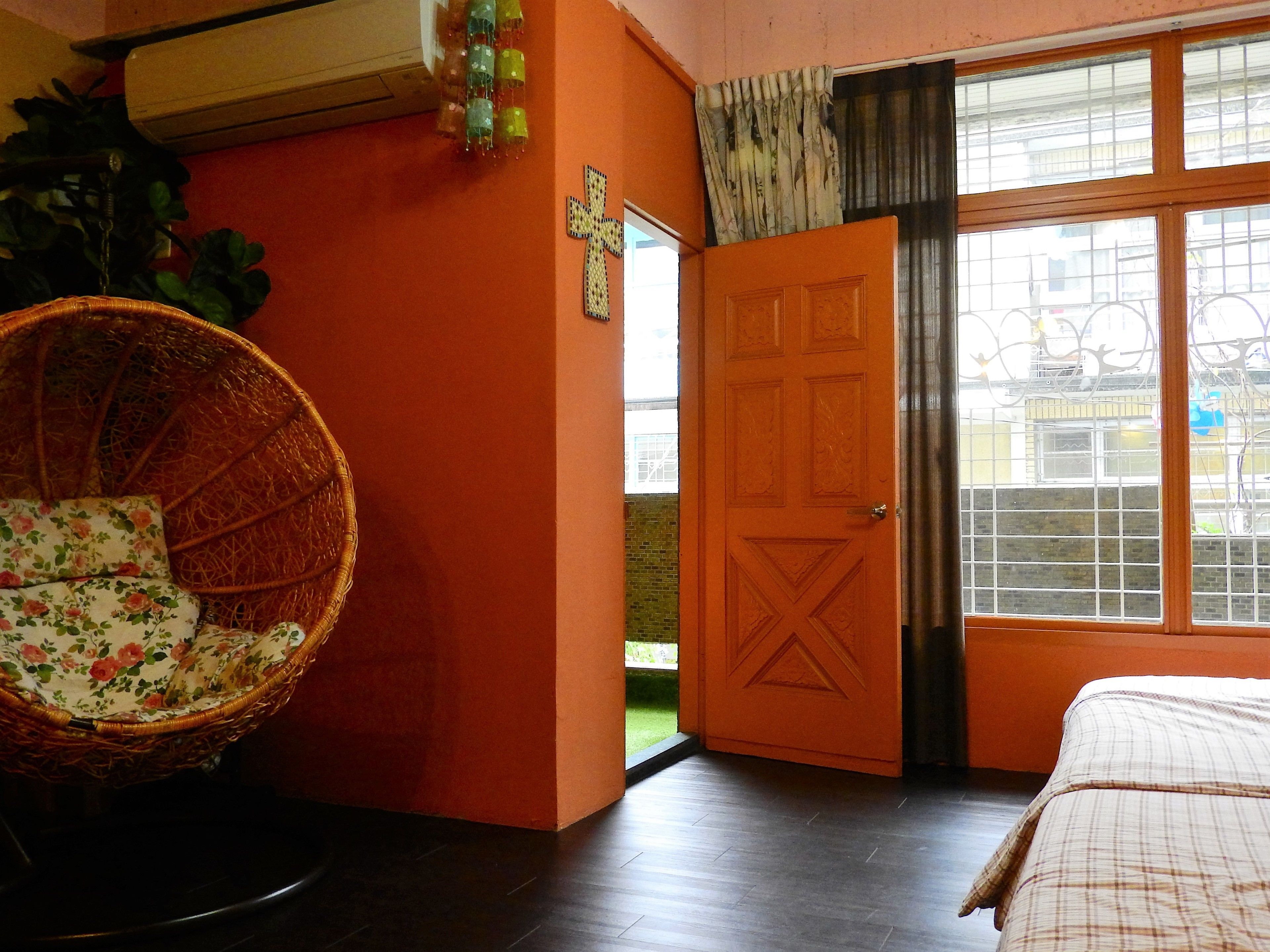Quarto com uma cadeira de vime, uma porta de madeira e vista para o exterior.