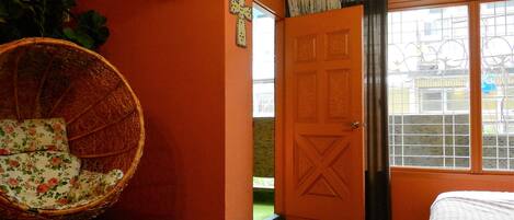 Quarto com uma cadeira de vime, uma porta de madeira e vista para o exterior.