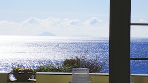 Vista do mar por uma janela, com uma planta em vaso e uma cadeira.