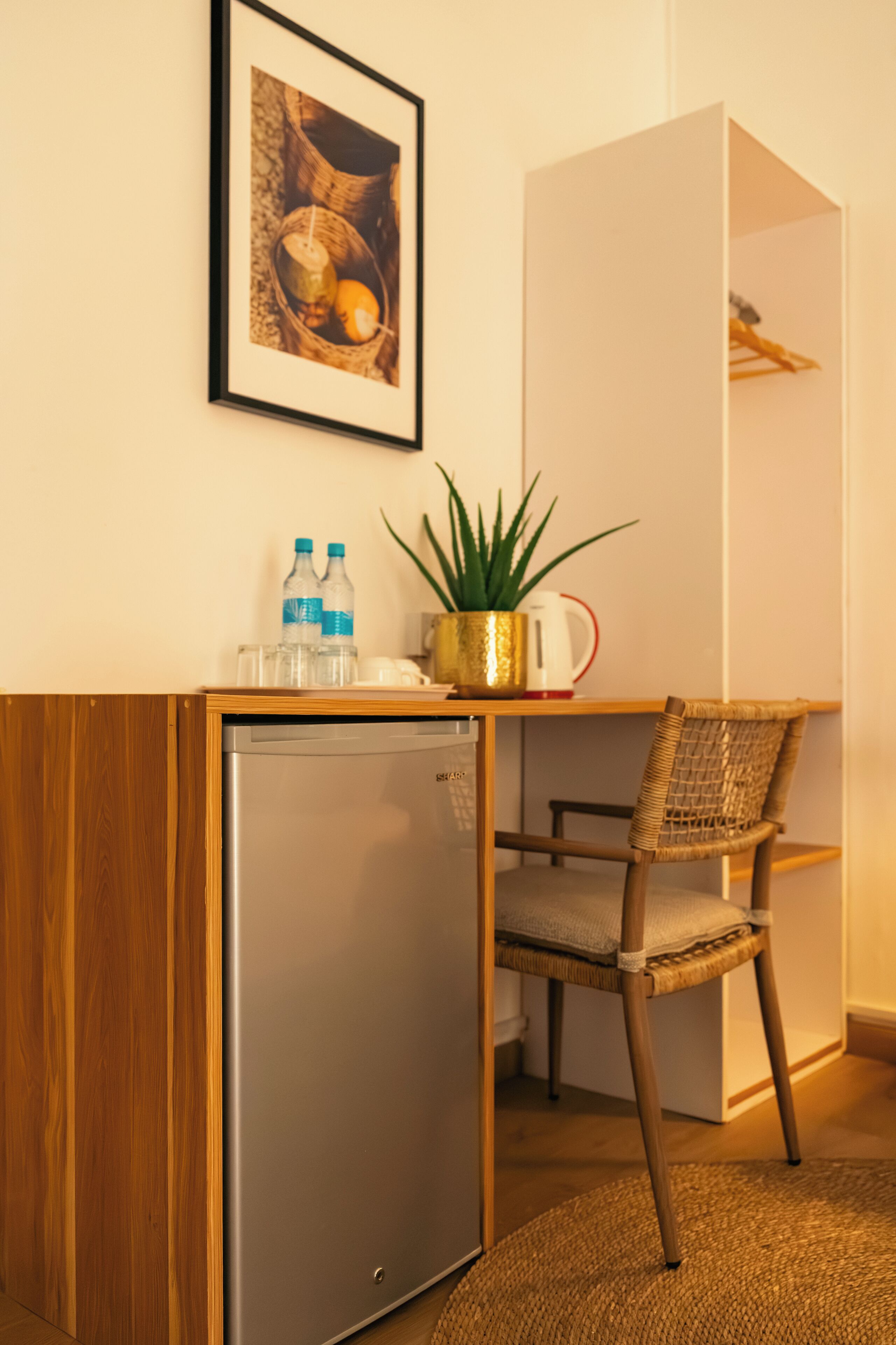 Uma cozinha compacta com geladeira, uma mesa pequena, uma cadeira, uma planta em vaso e um quadro na parede.