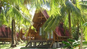Uma cabana de madeira com telhado de palha, rodeada por palmeiras e uma área gramada.