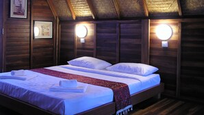 Uma cama de casal com lençóis brancos e um cobertor vermelho, duas luminárias de cabeceira, paredes de madeira e teto inclinado.