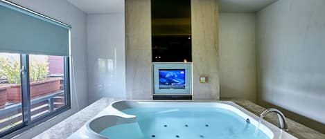 Casa de banho moderna com uma banheira grande, janela com vista e televisão na parede.