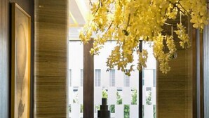 Um lobby moderno com piso de mármore polido, uma grande obra de arte emoldurada à esquerda e uma área de estar com sofá e poltronas.