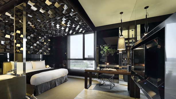 Quarto de hotel moderno com uma cama grande, uma escrivaninha e vista para a cidade.