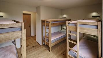 Quarto com beliches, piso de madeira e luminárias de cabeceira.