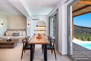 Uma área de refeições moderna com uma mesa e cadeiras de madeira, um sofá com almofadas e vista para uma piscina.
