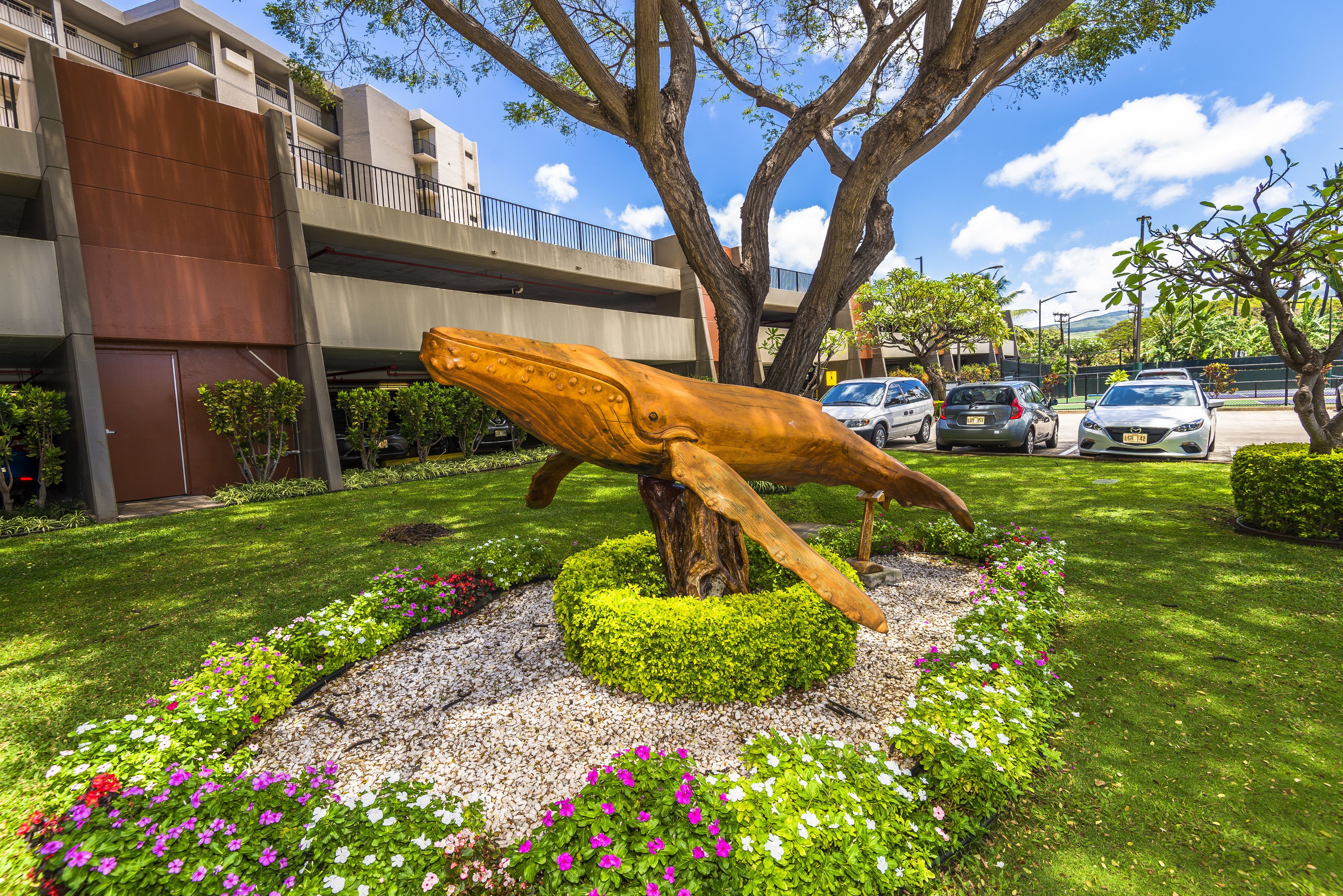 Escultura de baleia em um jardim paisagístico, com um edifício ao fundo.