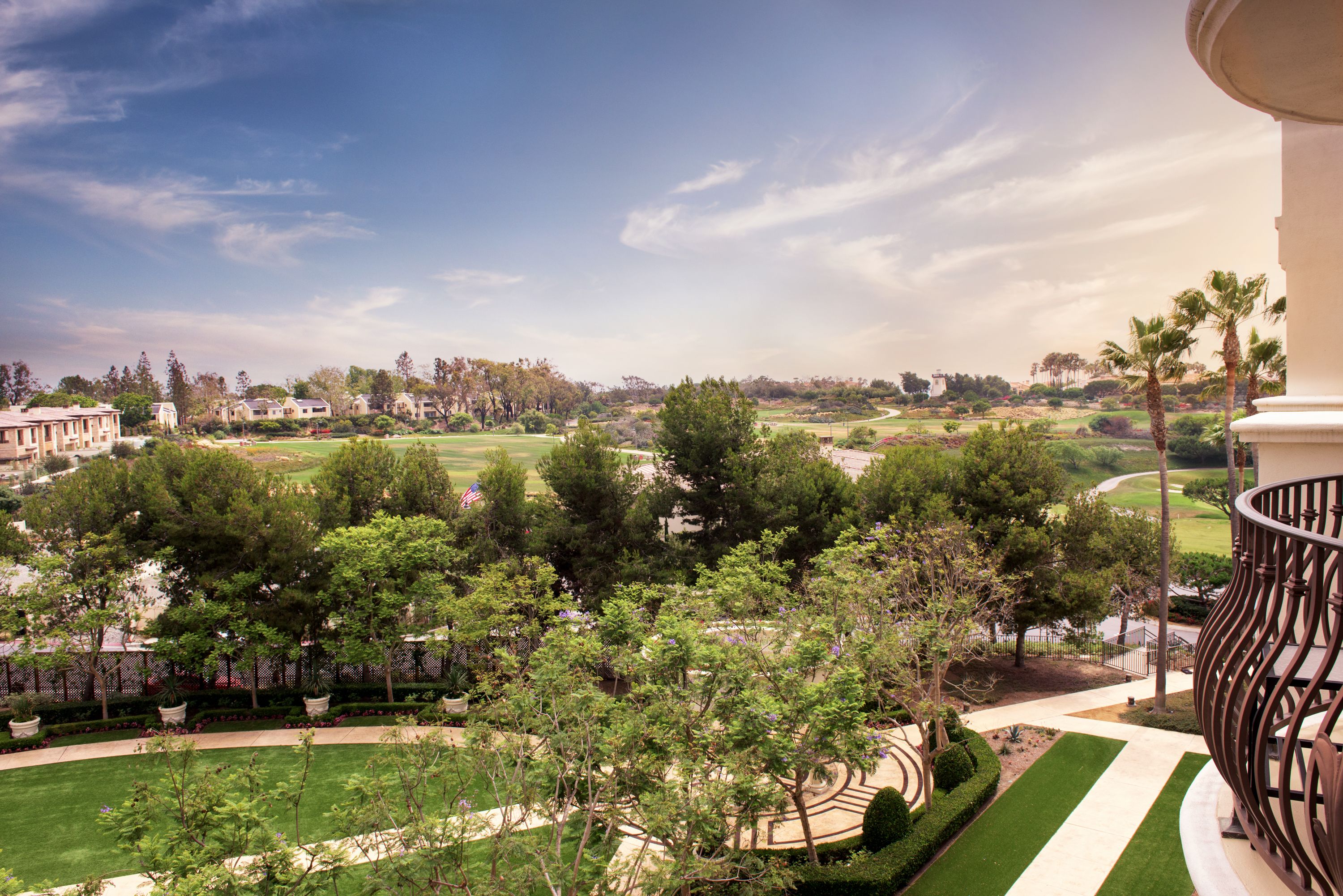 Uma varanda com vista para um jardim ajardinado, um campo de golfe e edifícios ao longe.