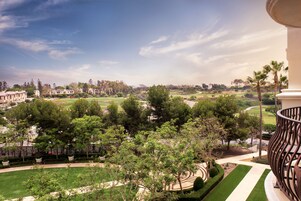 Uma varanda com vista para um jardim ajardinado, um campo de golfe e edifícios ao longe.