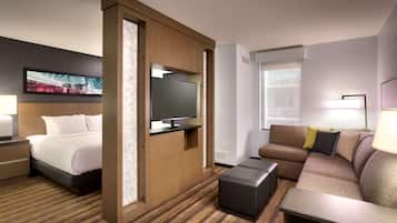 Quarto de hotel com cama, sofá, televisão e janela.