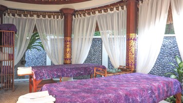 Um espaço de spa com duas macas de massagem, uma cadeira de madeira e uma parede de pedra.