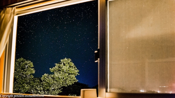 Uma janela com vista para o céu noturno, incluindo estrelas e árvores.