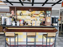Uma área de bar com balcão quadriculado, banquetas e diversos copos e garrafas.