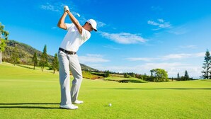 Um golfista num campo de golfe com céu azul límpido e grama verde.