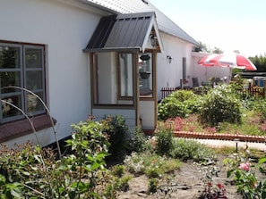 Uma casa com jardim, um guarda-sol vermelho e branco, e telhado de metal.