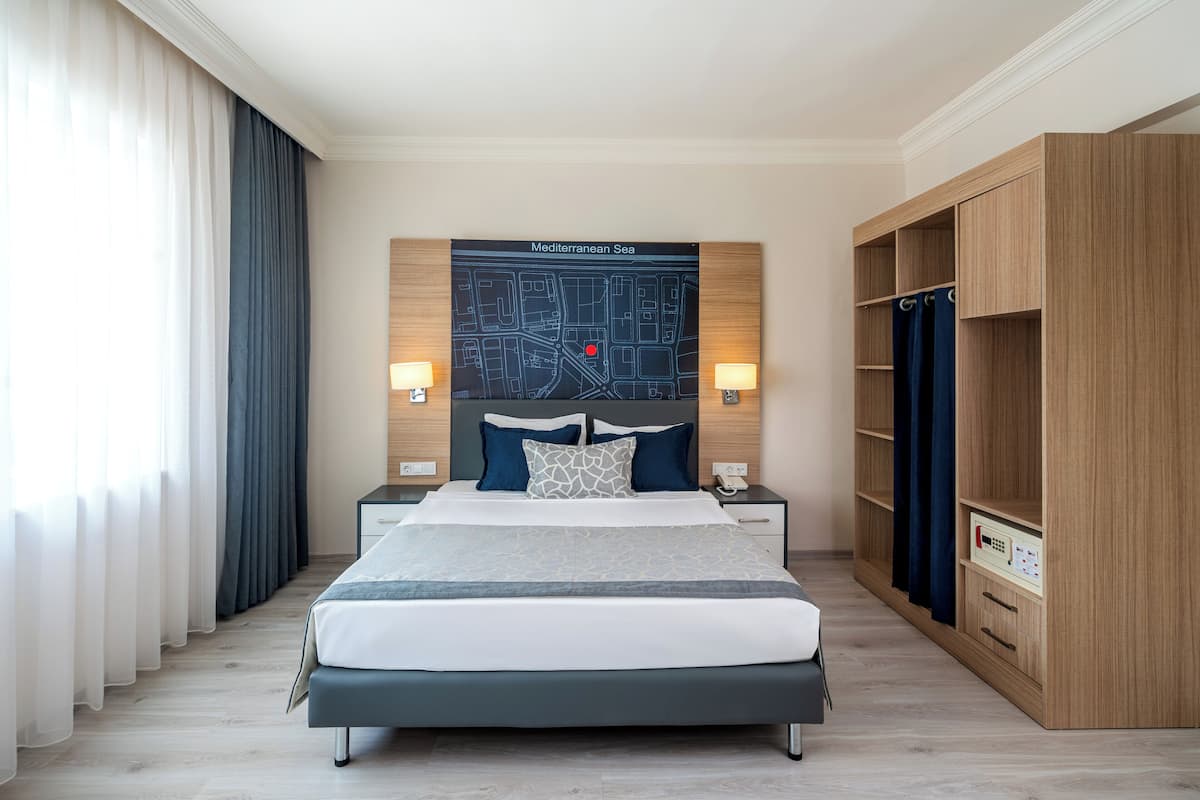 Quarto de hotel com uma cama grande, um mapa na parede, um guarda-roupa e uma mesa de cabeceira com abajur.