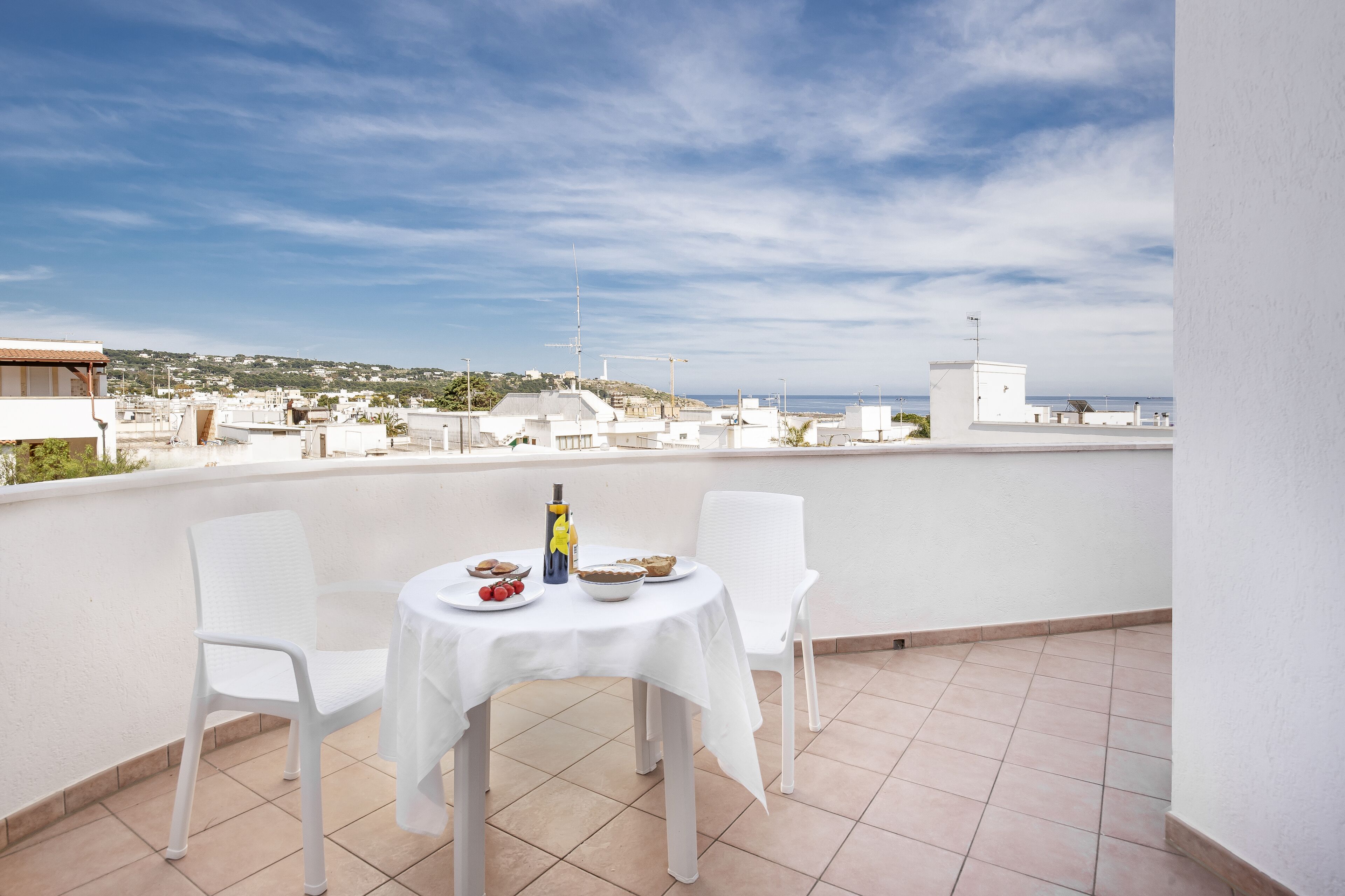 Terraço no terraço com uma mesa para dois, uma garrafa e uma cesta de frutas.