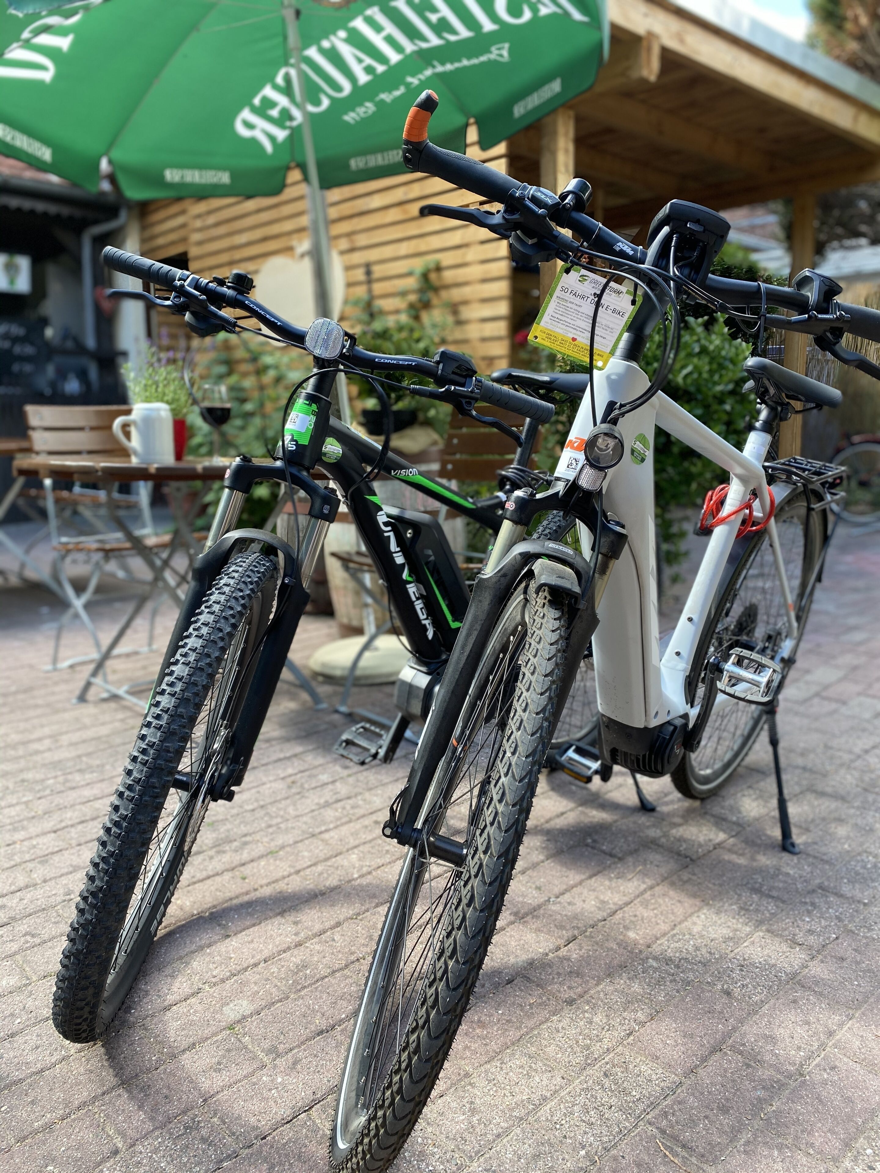 Uma bicicleta estacionada ao ar livre, com um guarda-chuva verde e uma estrutura de madeira ao fundo.