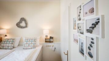 Quarto com cama, almofadas, luminária na parede, prateleira pequena com um telefone e quadros na parede.
