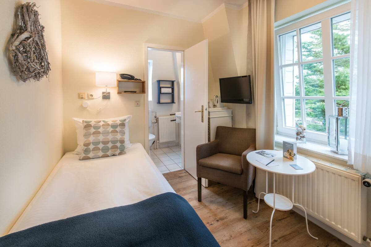Quarto com cama, poltrona, mesinha, televisão e janela com vista.