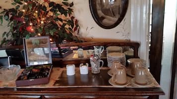 Uma mesa de buffet com pratos, copos e um jarro, cercada por um espelho e uma planta com luzes.