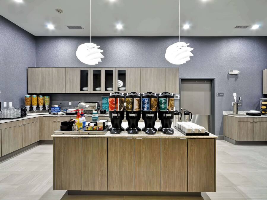 Cozinha moderna com ilha central, equipada com várias máquinas de café, uma pia e bancada com diversos objetos.
