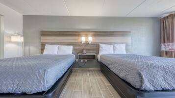 Quarto de hotel com duas camas, uma mesa de cabeceira com duas luminárias e uma cabeceira de madeira.