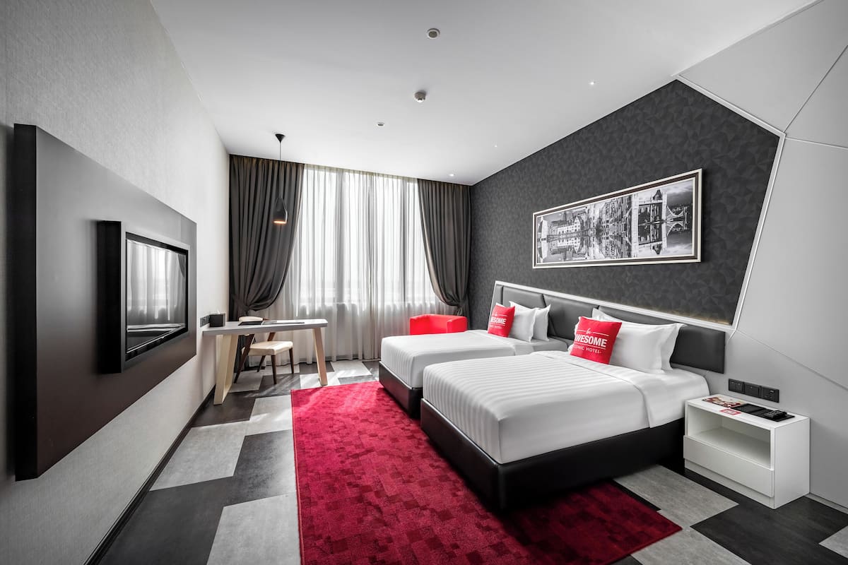 Quarto de hotel moderno com duas camas, uma escrivaninha e uma janela grande com cortinas.