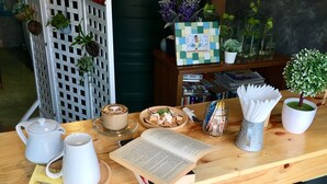 Uma mesa de madeira com um livro, um bule, uma chávena, uma tigela de comida e uma pequena planta em vaso.