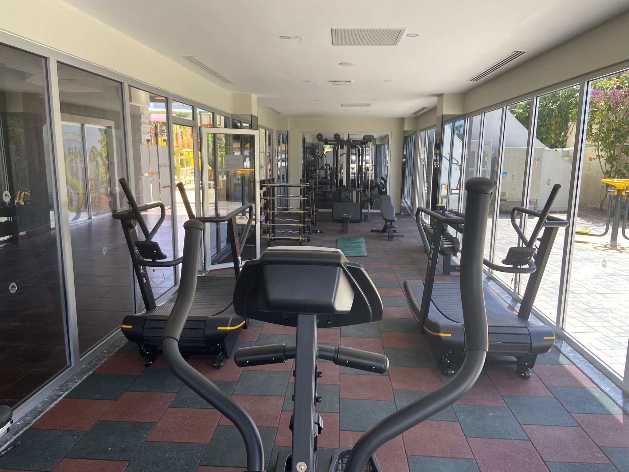 Uma academia com equipamentos de ginástica, grandes janelas e piso revestido de azulejos.
