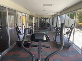 Uma academia com equipamentos de ginástica, grandes janelas e piso revestido de azulejos.