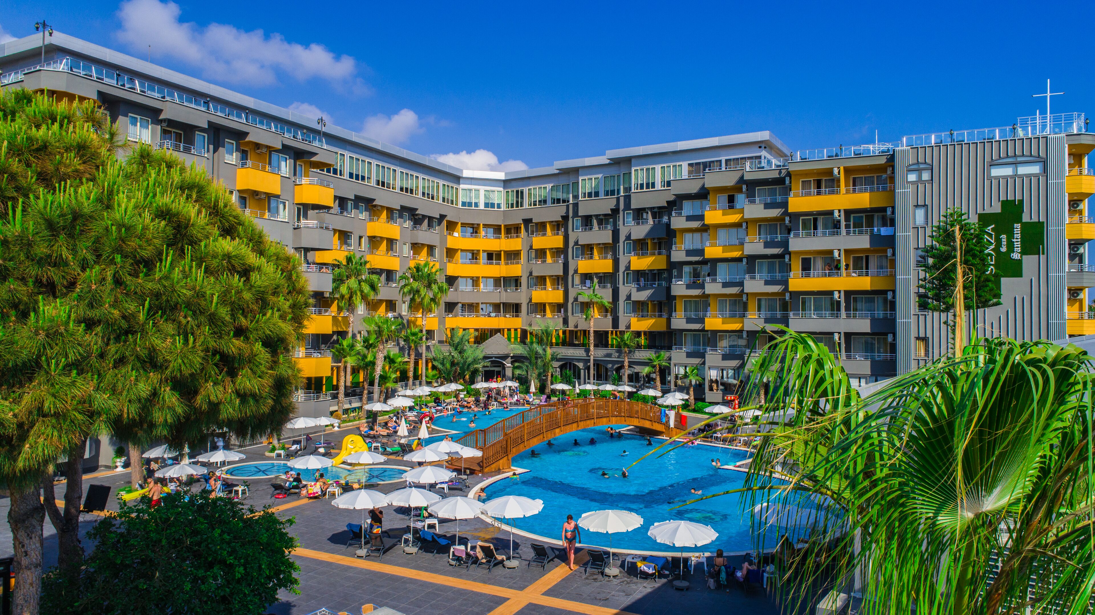 Hotel com várias varandas, área de piscina central e vegetação ao redor.