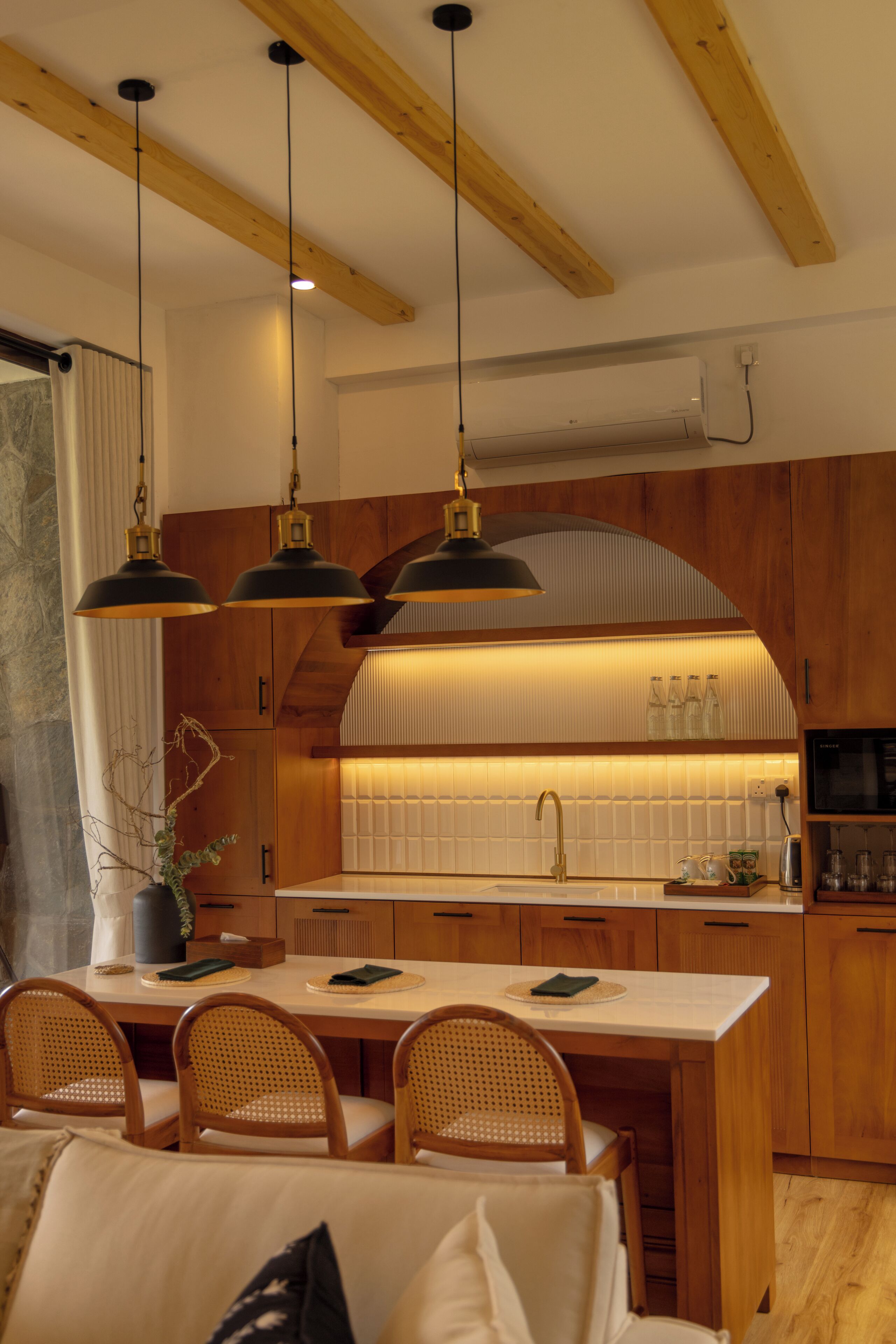 Uma cozinha moderna com armários de madeira, uma ilha central, iluminação pendente e uma área de refeições com cadeiras de vime.