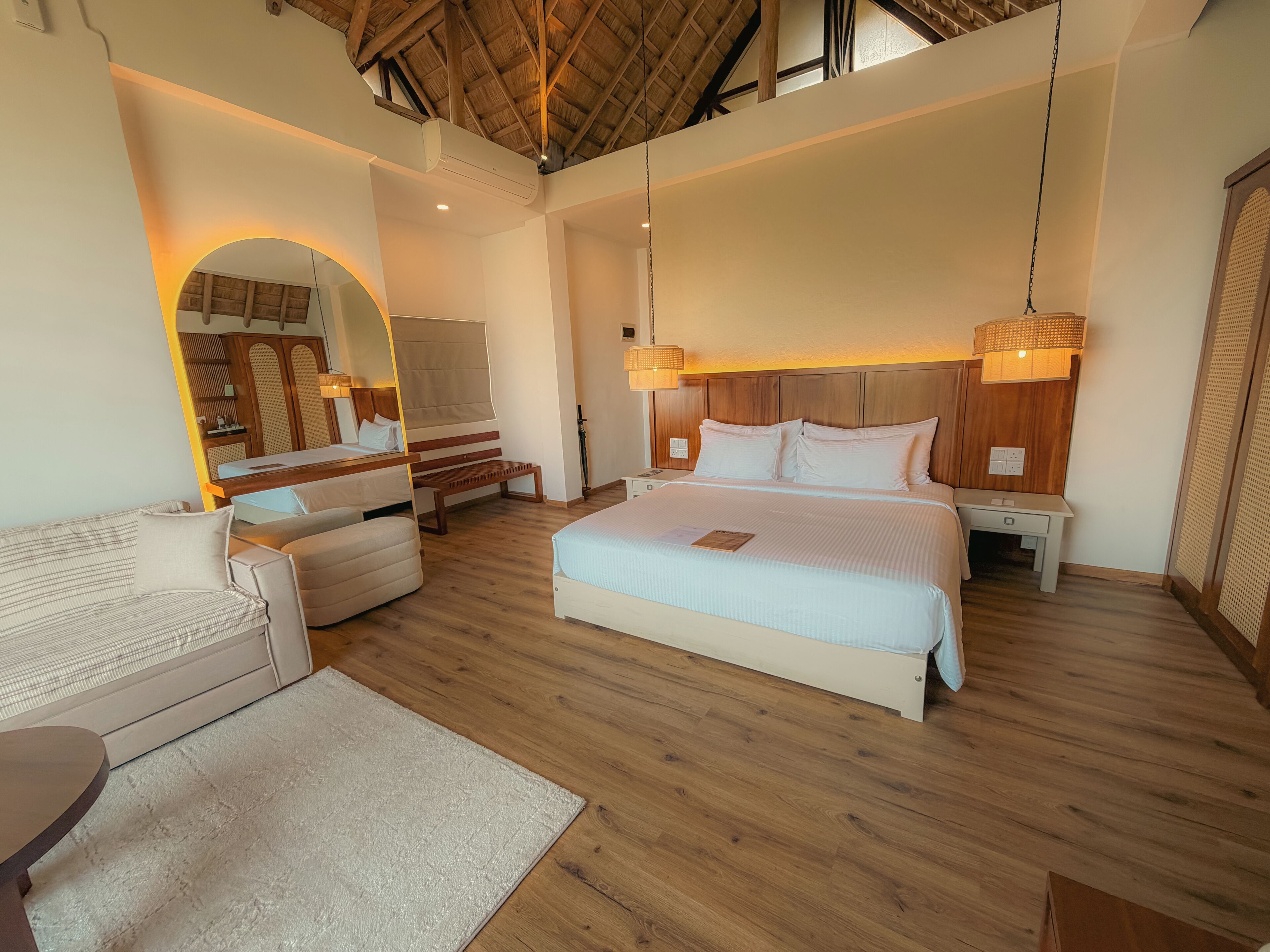 Um quarto espaçoso com uma cama grande, um sofá, uma escrivaninha e um espelho.