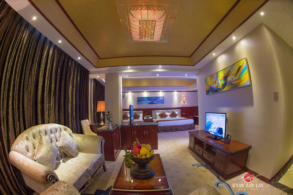 Quarto de hotel espaçoso com uma cama grande, televisão, escrivaninha e um espaço de estar confortável.