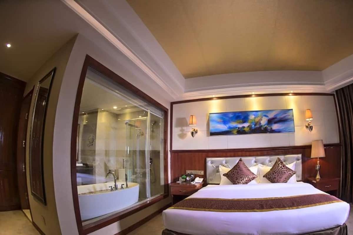 Quarto de hotel com cama grande, chuveiro em cabine de vidro, televisão fixada na parede e um quadro.