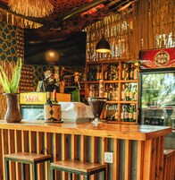 Uma área de bar com balcão de madeira, banquetas, uma televisão e prateleiras cheias de garrafas.