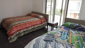 Quarto com duas camas, uma mesa pequena e janelas amplas.