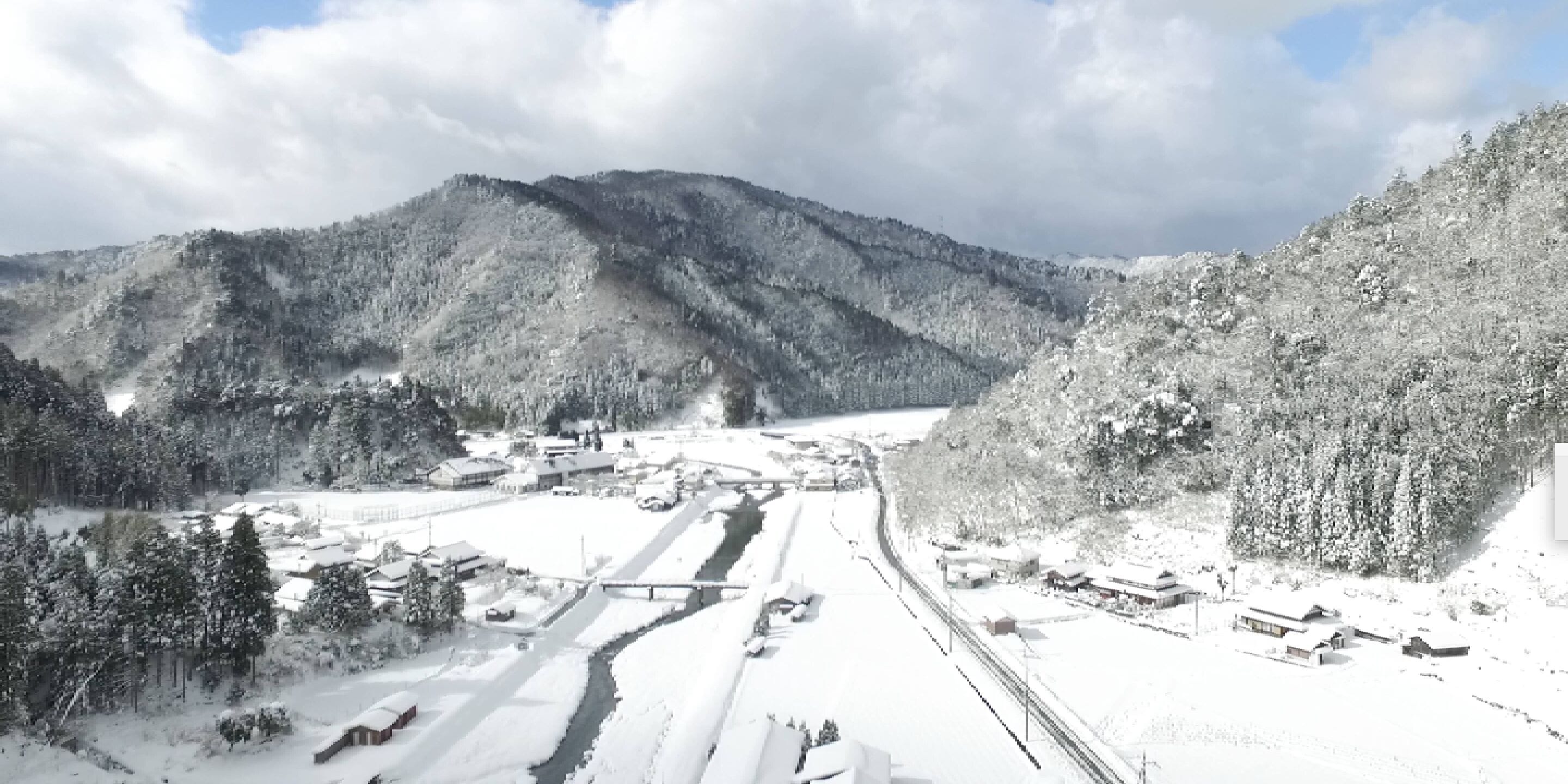 Paisagem coberta de neve com rio, montanhas e uma ponte.