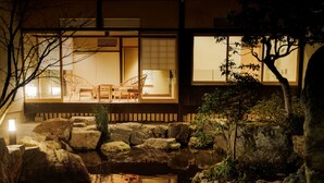 Um edifício tradicional em estilo japonês, com pisos de esteira de tatame, um lago de carpas koi e um deck de madeira com cadeiras.