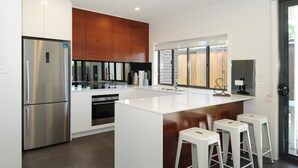 Uma cozinha moderna com geladeira de aço inoxidável, uma ilha central com banquetas, armários de madeira e uma janela grande que oferece iluminação natural.