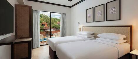 Quarto de hotel com duas camas, um ventilador de teto, televisão e varanda com vista para palmeiras.